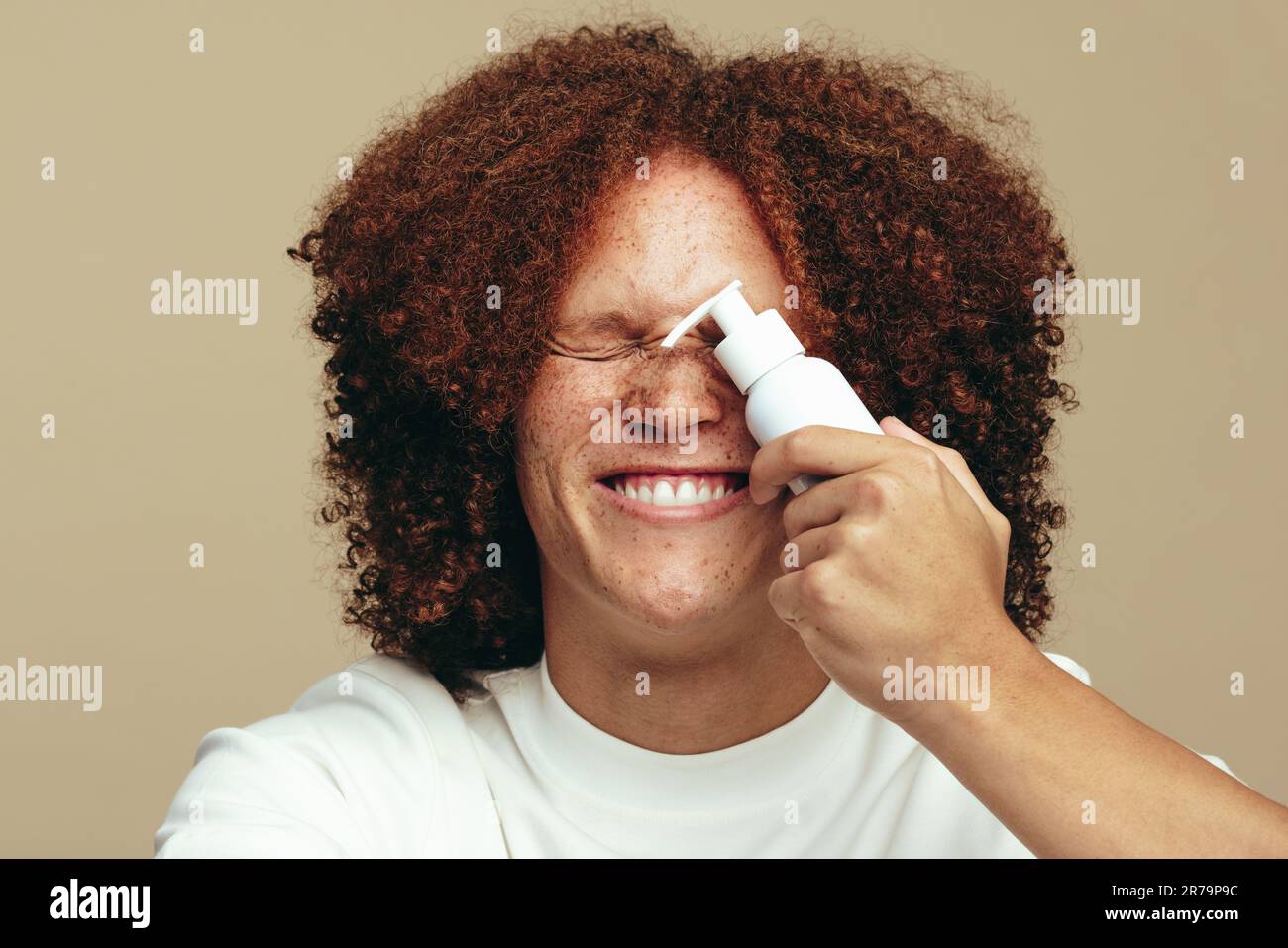 Man with a ginger afro smiling happily while holding a bottle of facial ...