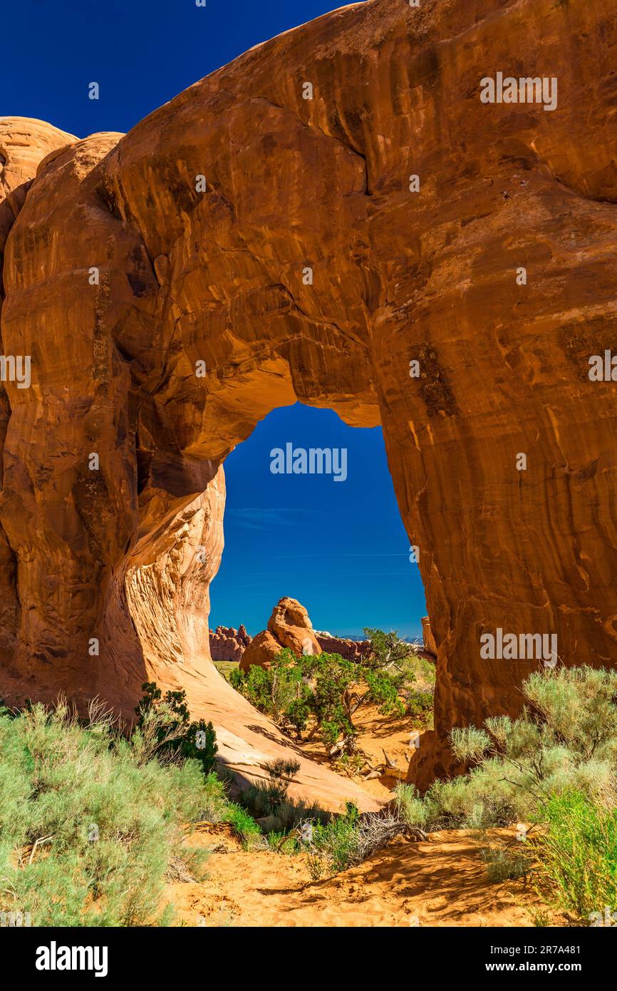 An elegant rock arch formation stands tall under a blue sky in Arches ...