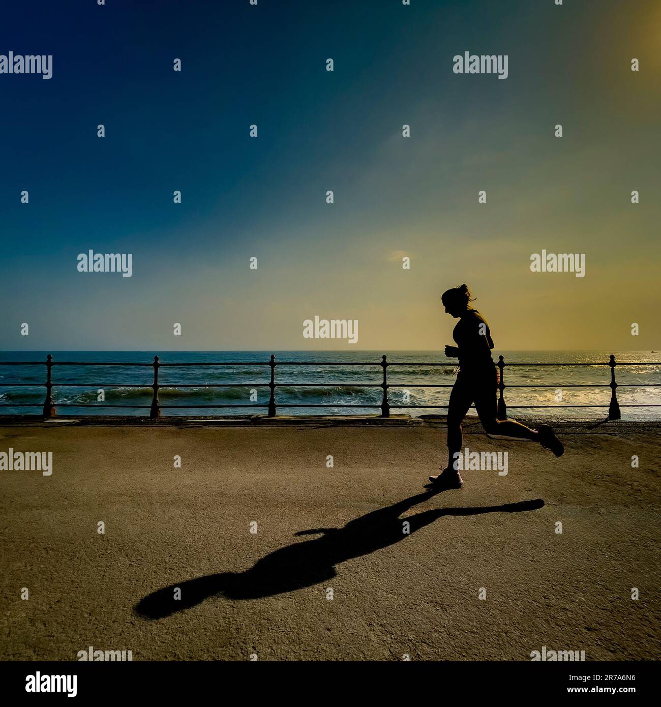 Silhouette of a female runner on Scarborough seafront as the sun rises ...