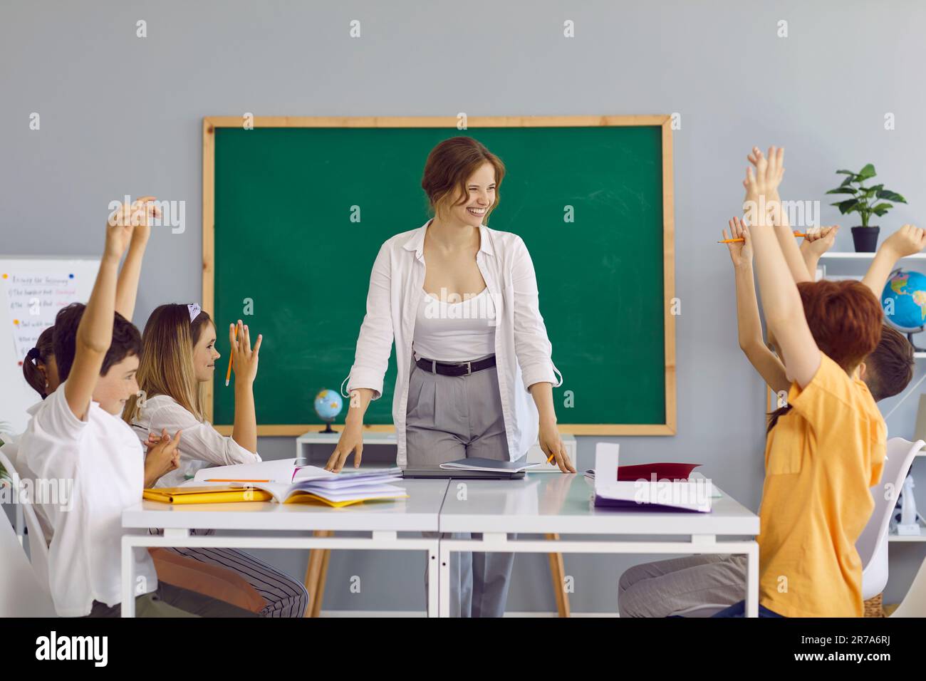 Children rising hands to answer teacher question sitting at desk in ...