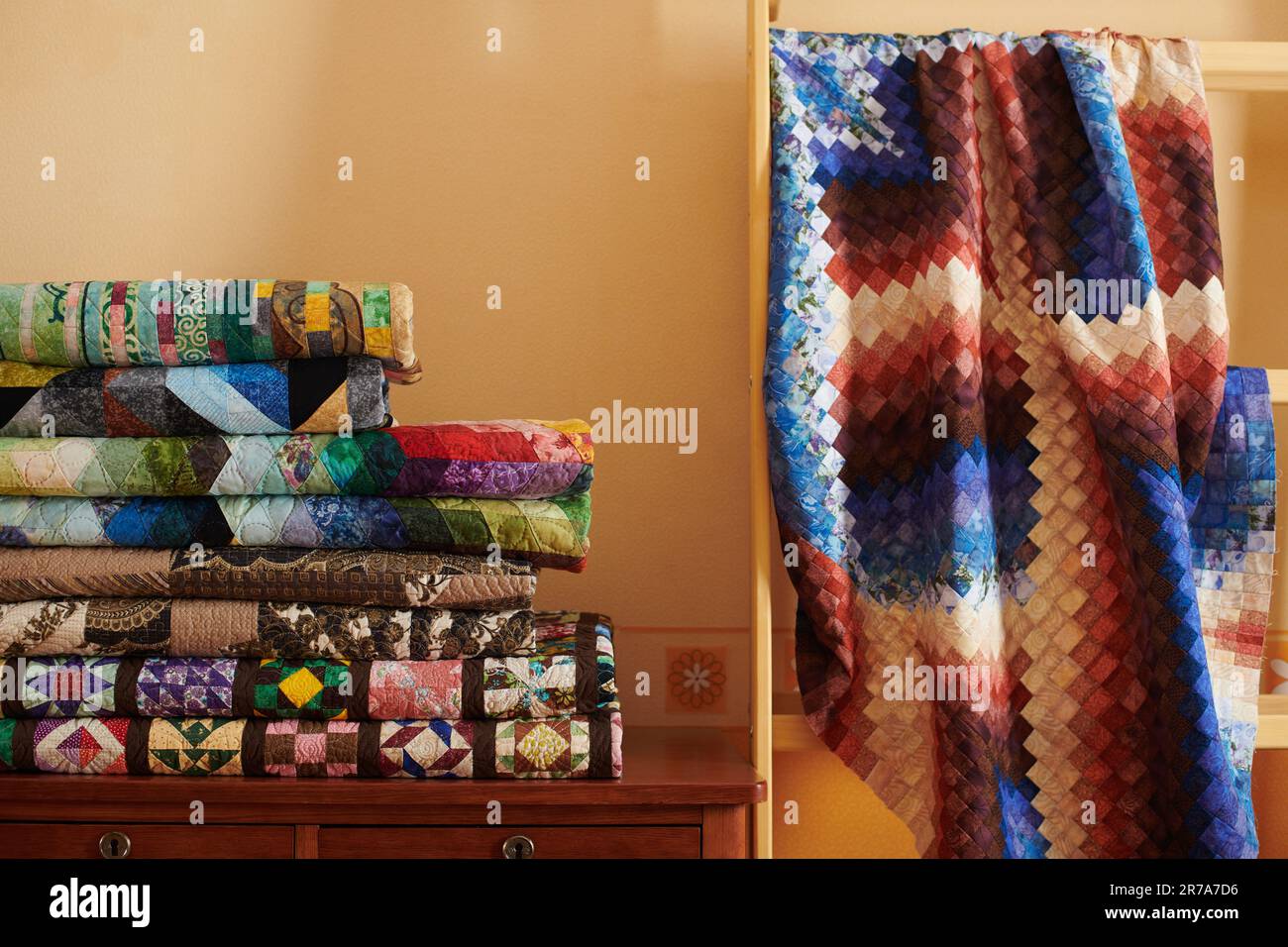 Stack of quilts and quilt made in the bargello style on yellow wall ...