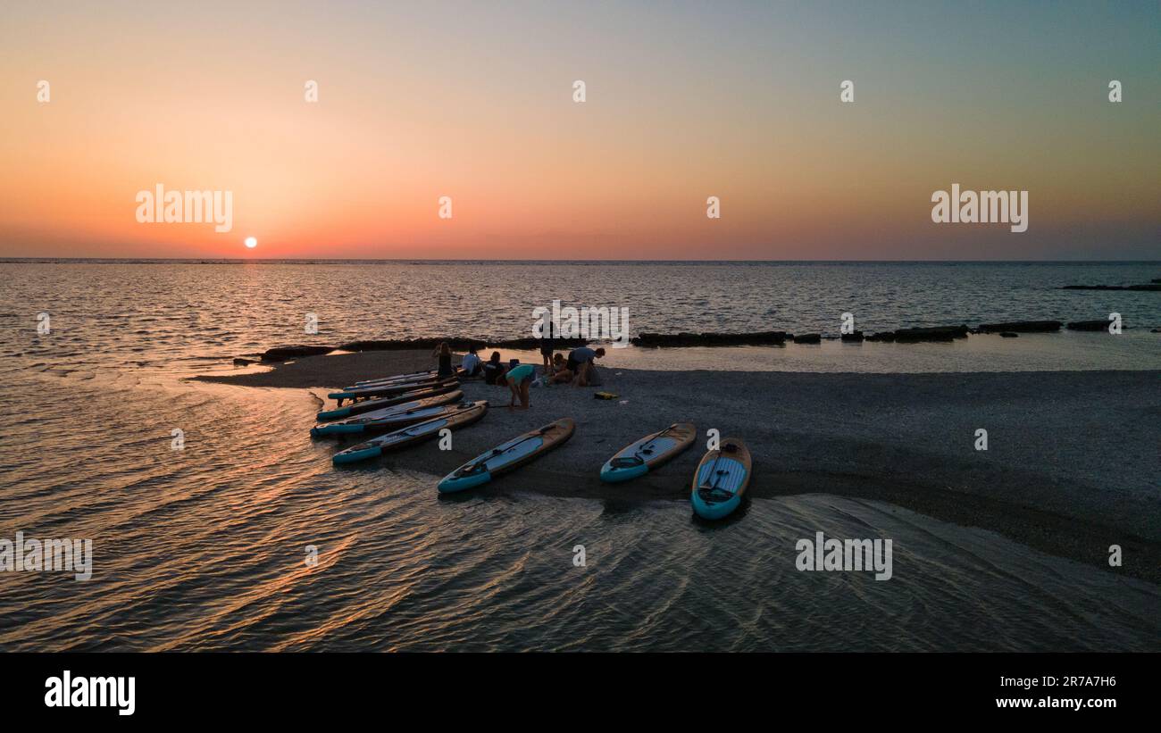 A collection of surfboards lined up along the shoreline as the sun sets ...