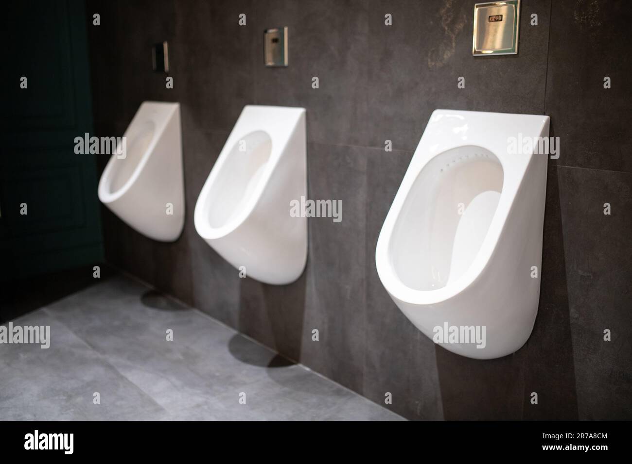 Three white urinals hanging on the wall in a dark luxury public toilet ...