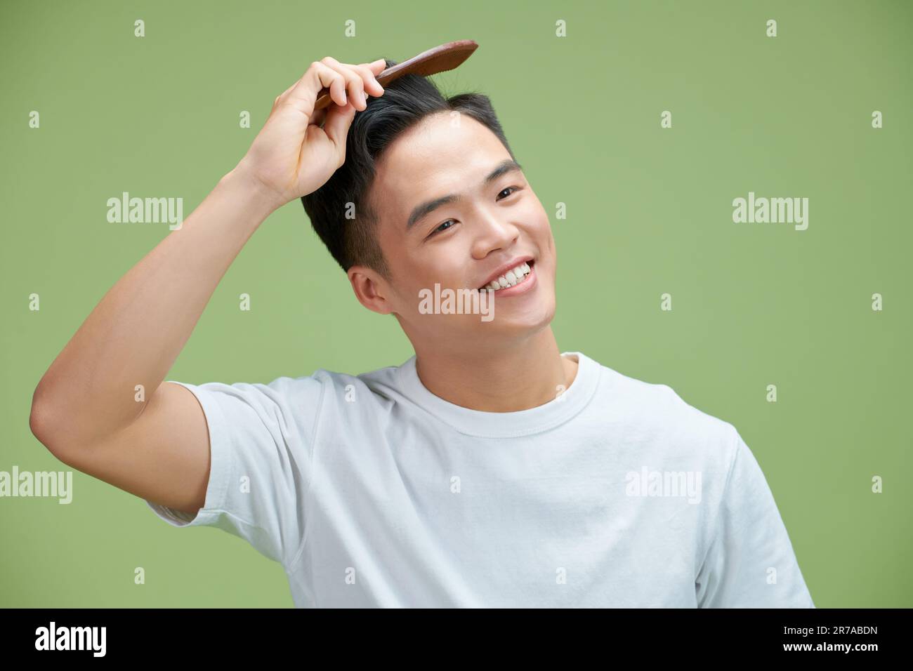 people concept - smiling young man brushing hair with comb on green ...