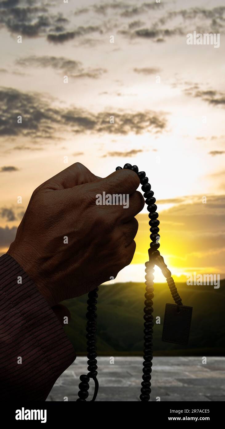 Muslim man praying with prayer beads in his hands with the sunset scene ...