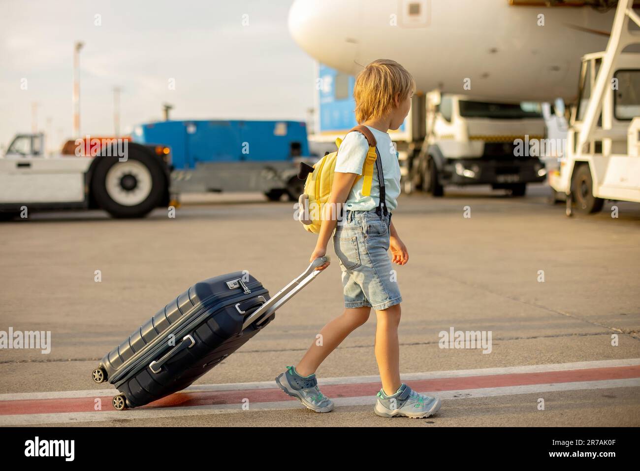 Cute blond child, kid with backpack, boarding airplane at the airport ...