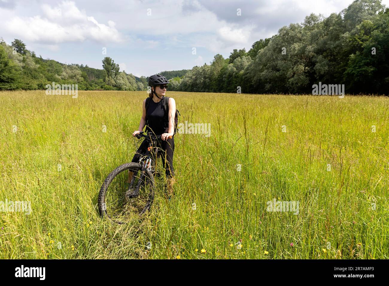 Tourist, a woman cyclist on a mountain bike, standing on a meadow ...