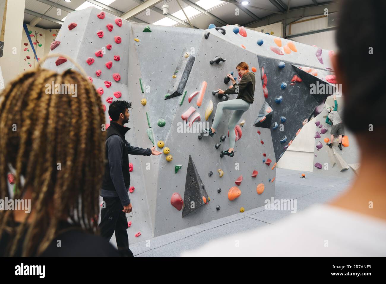 Group of friends being instructed by male coach at indoor wall climbing ...