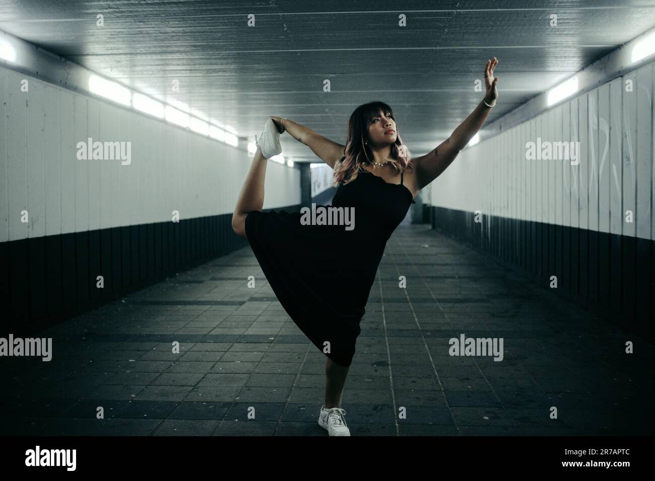 A young female stands in an illuminated tunnel, one arm draped around ...