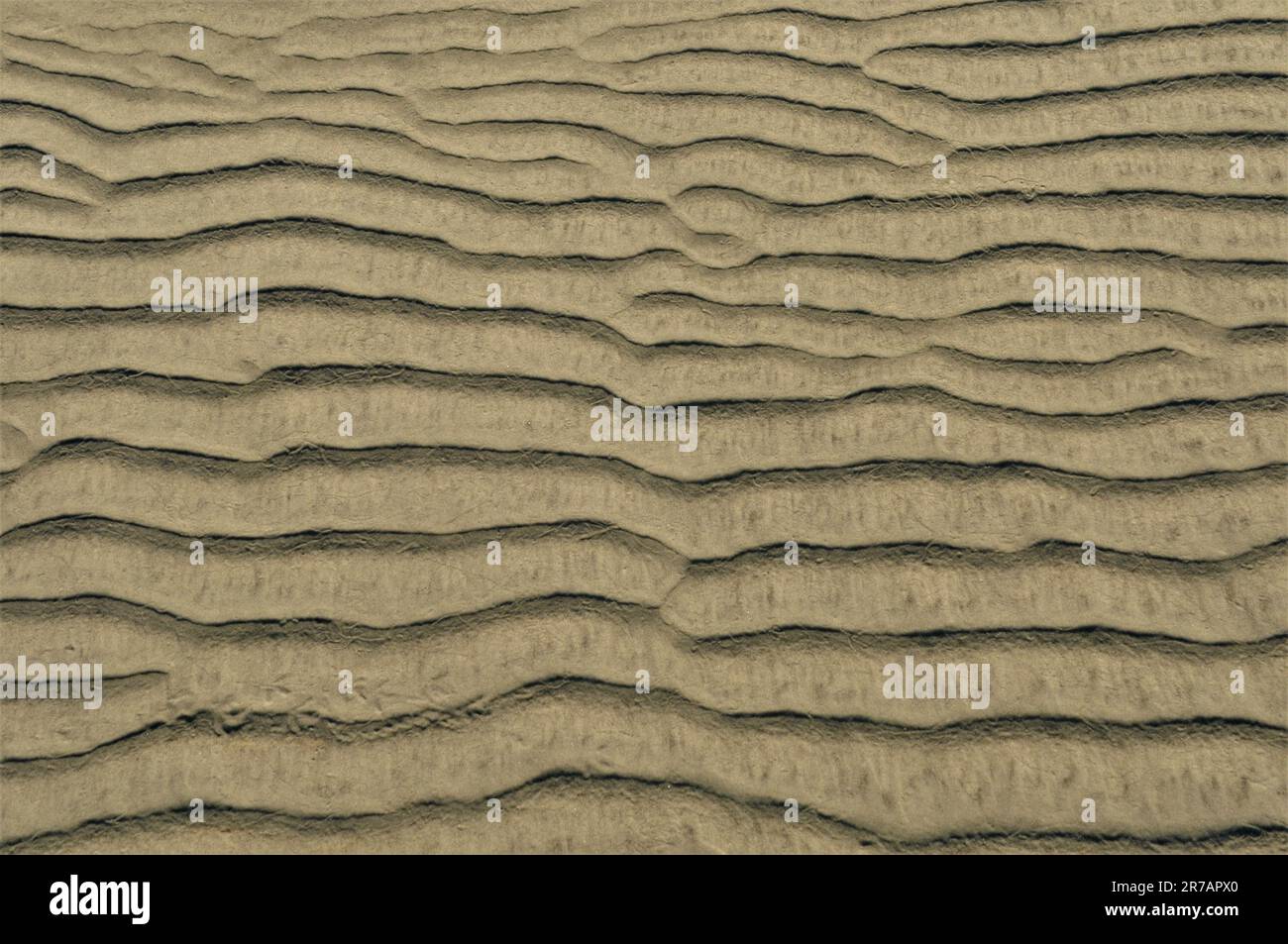 A close-up of a beach with a wave pattern imprinted on the wet sand ...