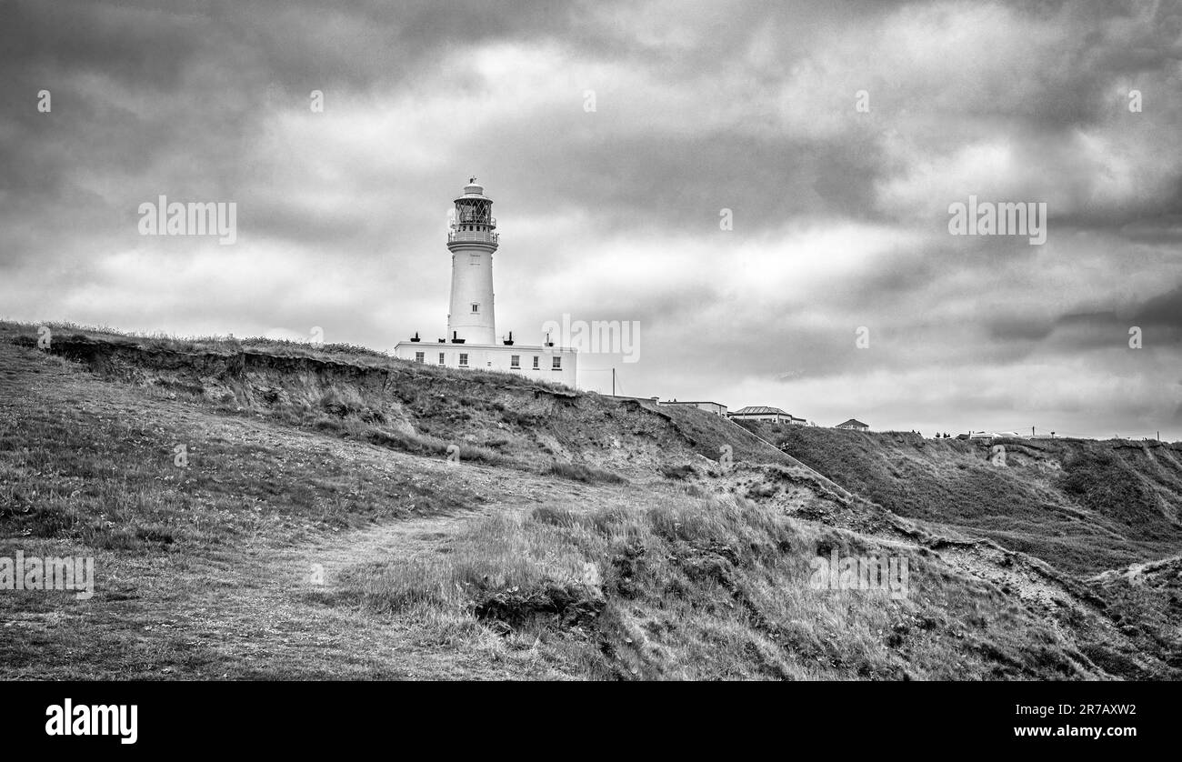 Steep cliffs lead up to Flamborough Head lighthouse. A cloudy sky is ...