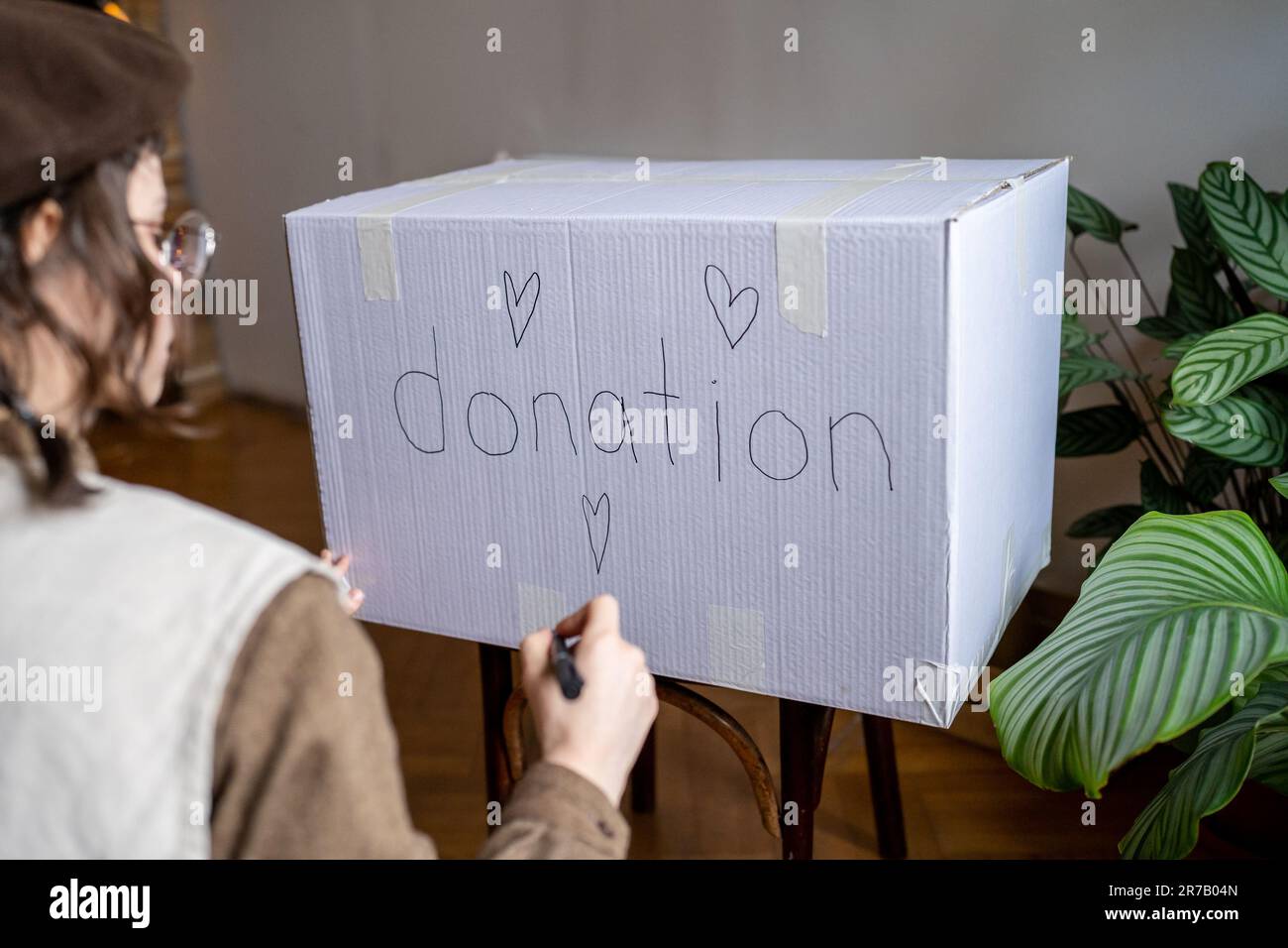 Millennial girl writing word donation on cardboard box while sorting ...