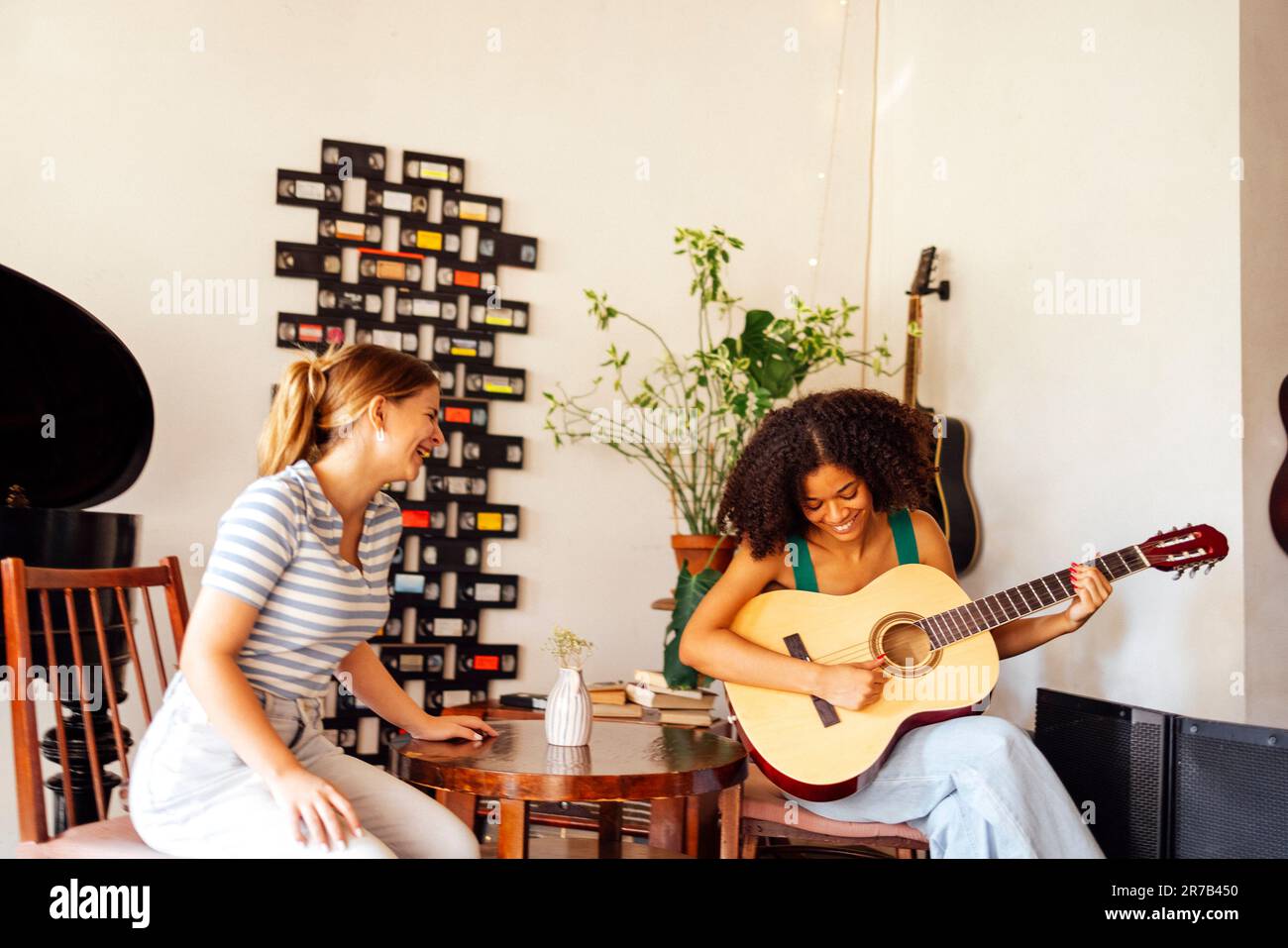 Two Laughing Multiracial Cute Girls Are Sitting In A Music Store Or A Retro Cafe Pretty African
