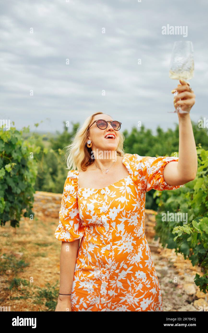 Cheerful blonde woman in bright orange dress with floral print holds ...