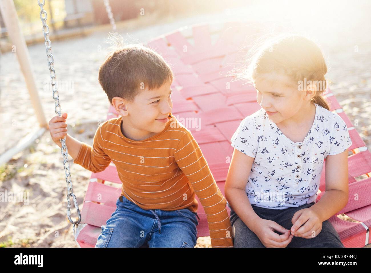 Cute little children ride on a pink wicker swing. Cheerful boy and girl ...
