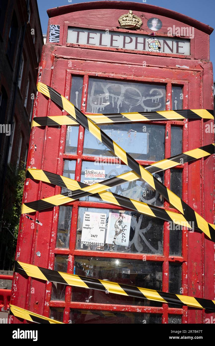 Hazard tape is wrapped around the doors of an old-style phone box od ...