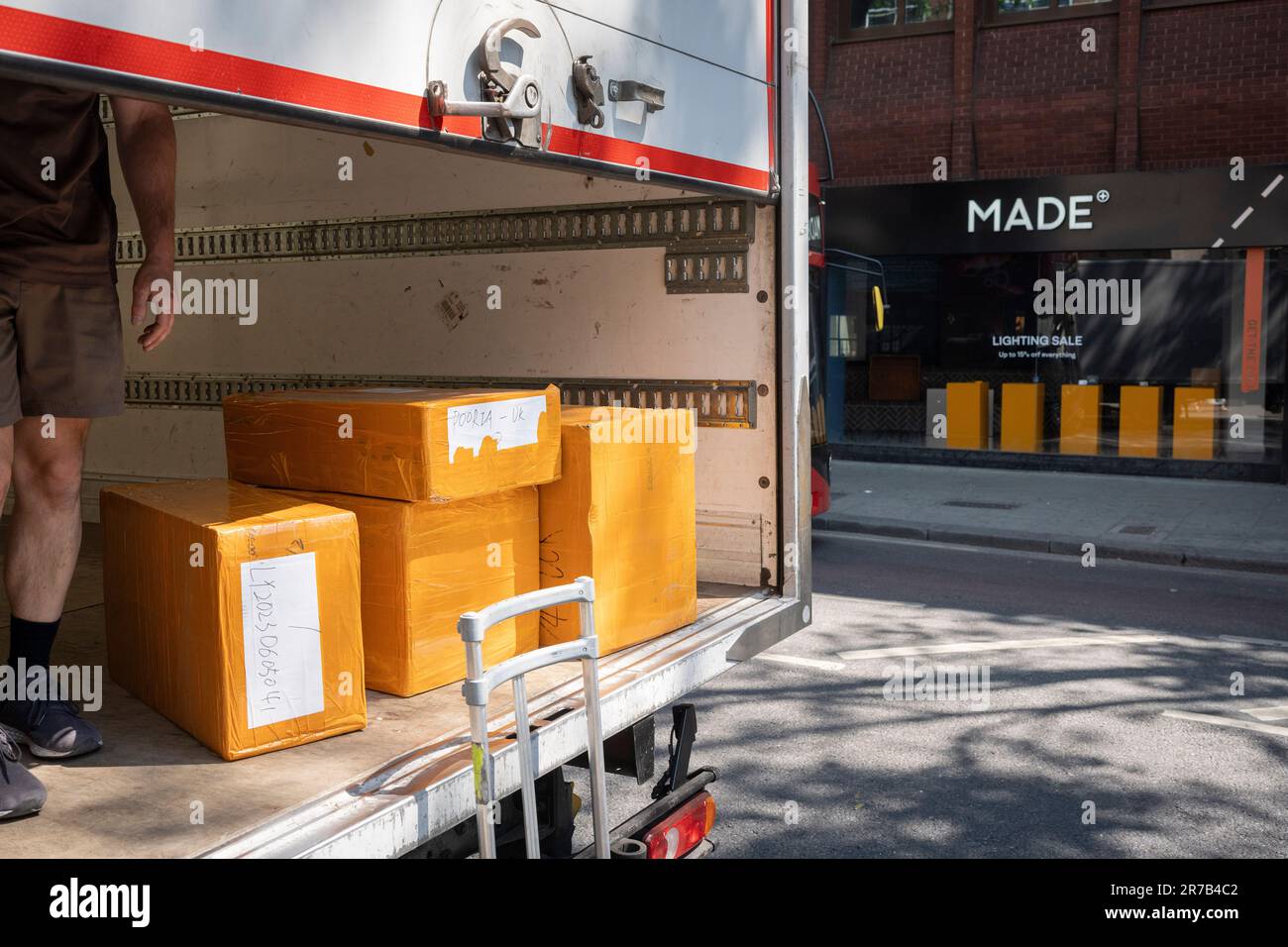 A UPS van driver unloads a stack of boxes from the rear of his vehicle ...