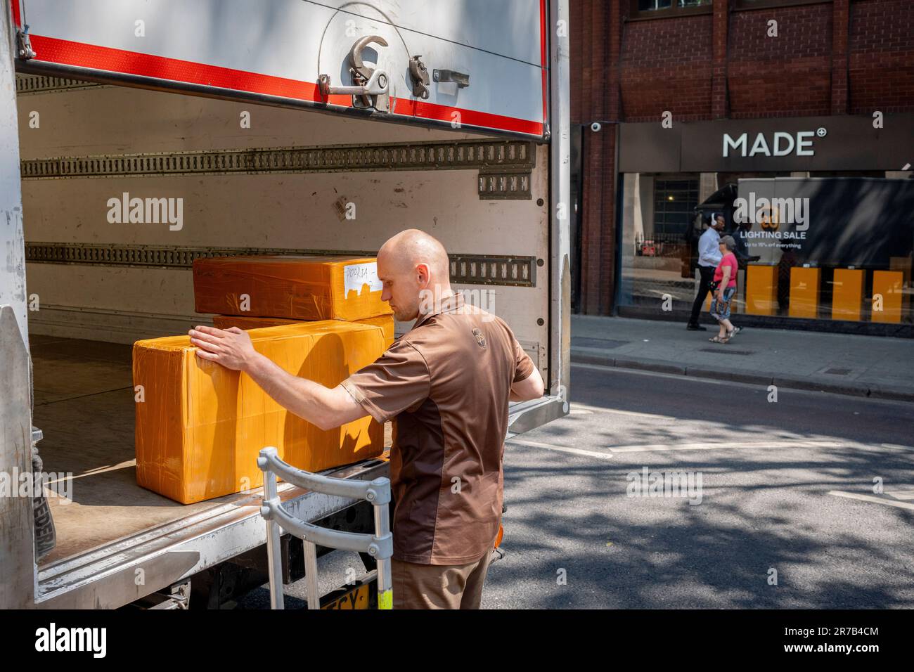 A UPS van driver unloads a stack of boxes from the rear of his vehicle ...