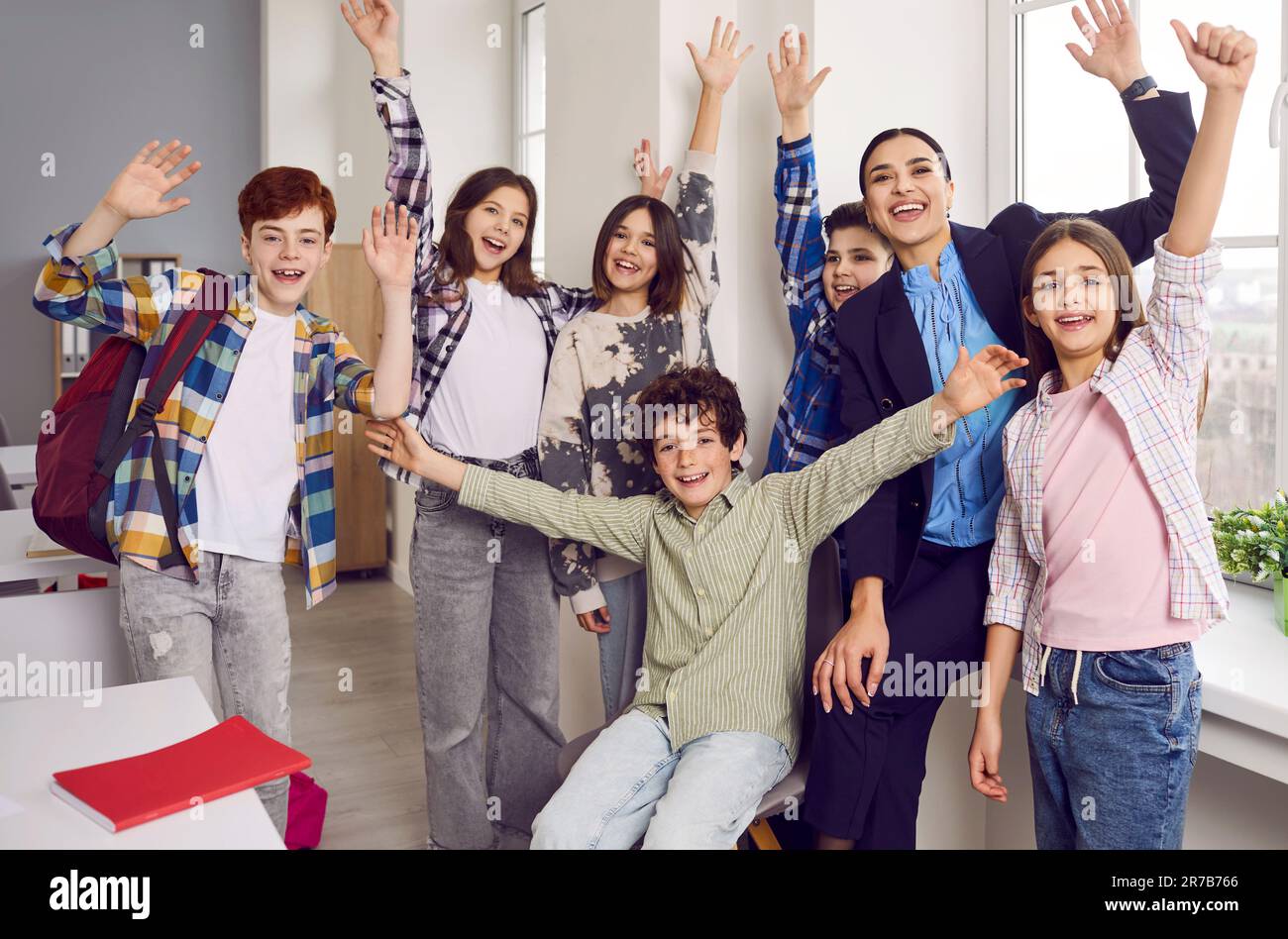 Happy schoolchildren with teacher looking at camera and waving hands in ...