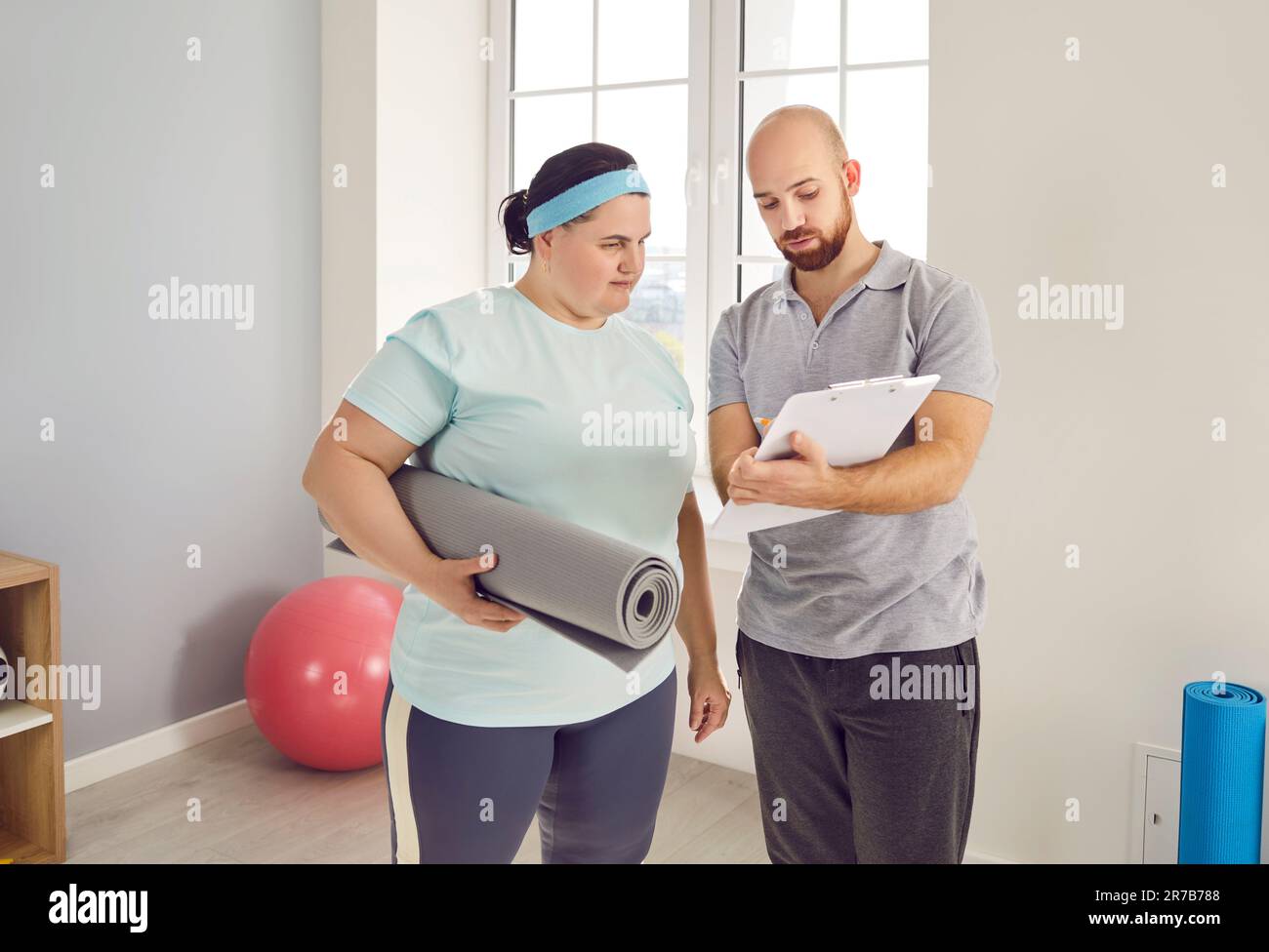 Plus size woman talking with personal trainer about her fitness program ...