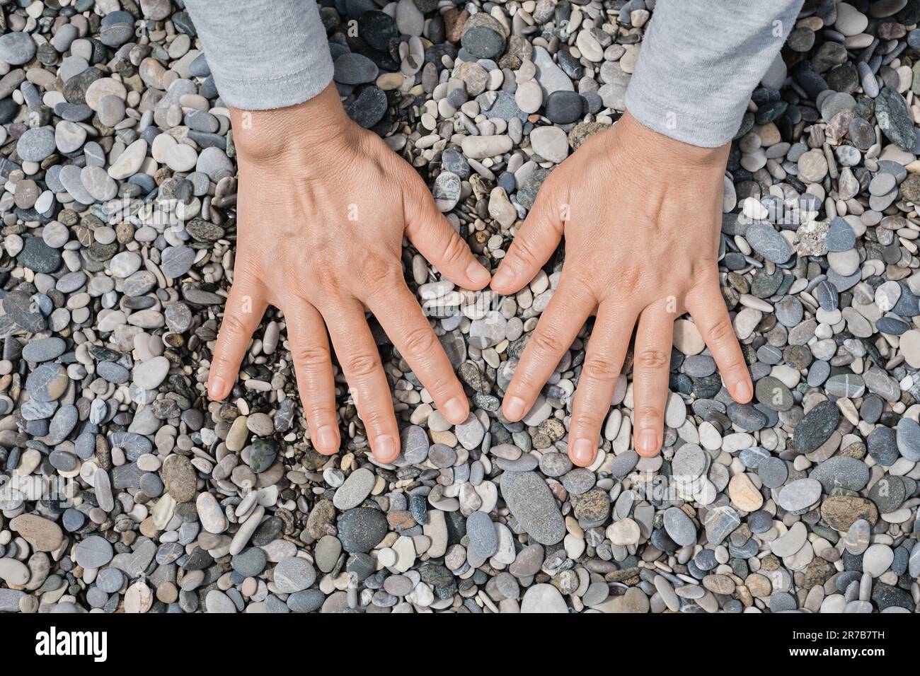 Women's hands lie on the sea pebbles. Pebble sea beach close up, dark ...