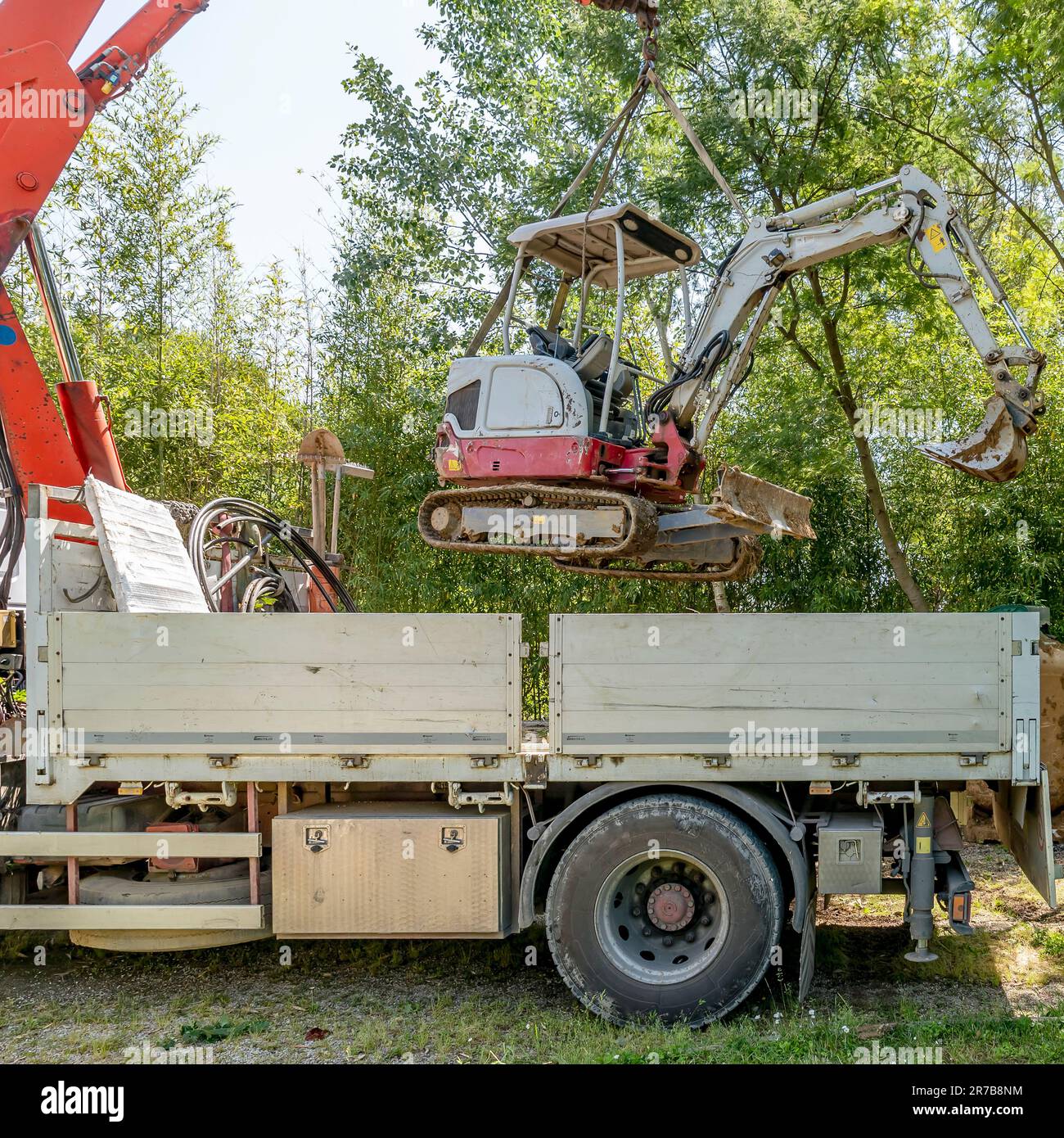 An excavator is lifted from a truck trailer with the help of a crane ...