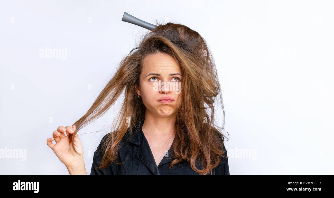 Sad woman combing styling tangled dry weak hair on a white background ...