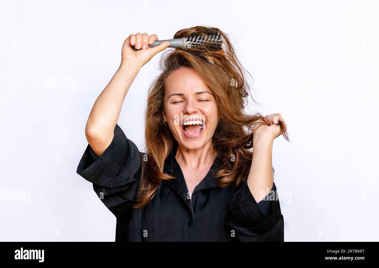 Brunette woman has fun laughing while styling her hair with hair comb ...