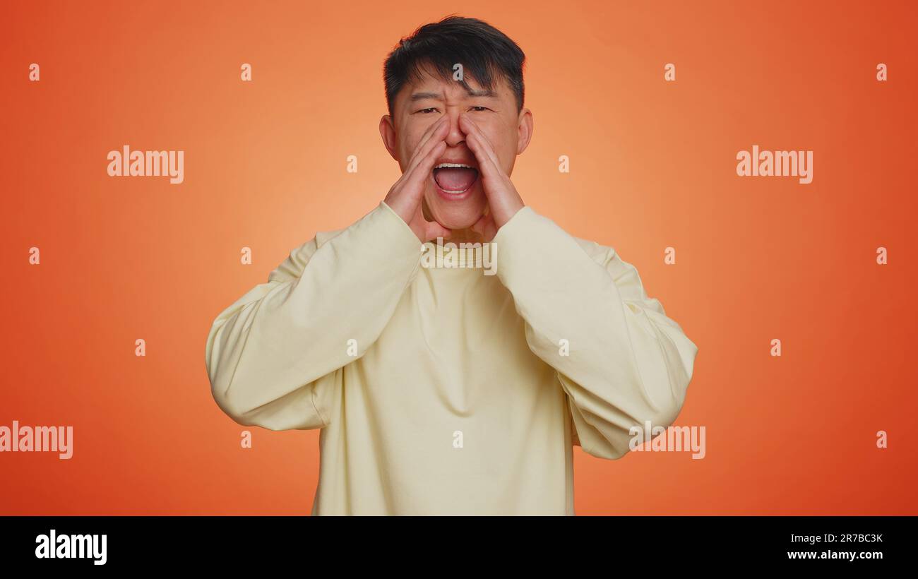 Asian handsome man scream yell with hand near mouth greeting with hand ...