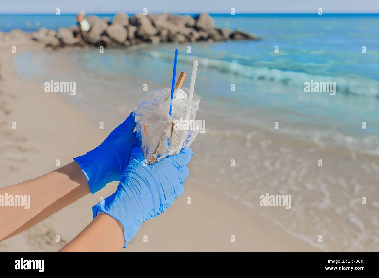 A man's hands hold a plastic bag of garbage against the beach and the ...