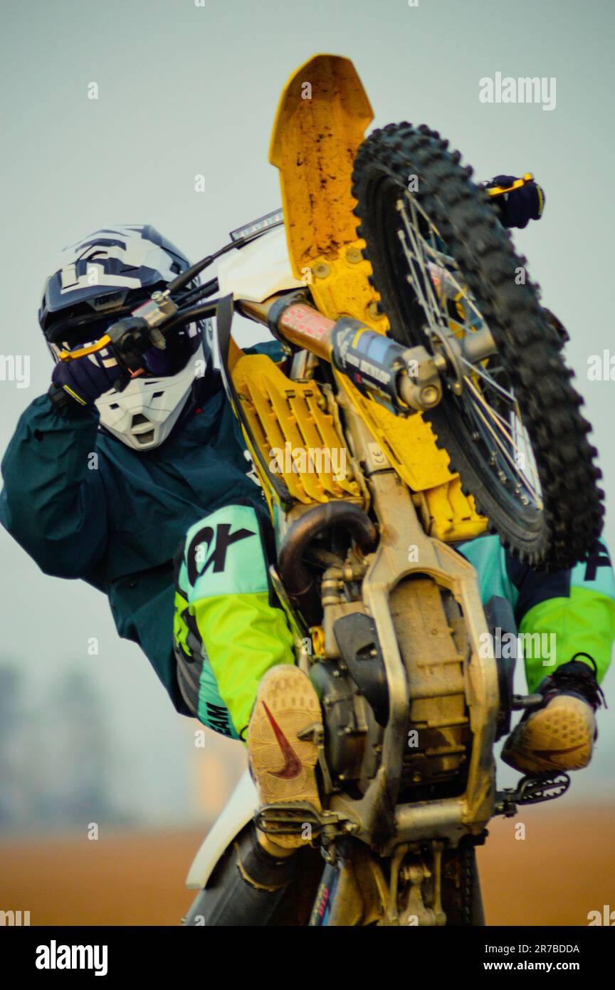 A man riding a dirt bike through a dusty terrain, wearing a full-face ...