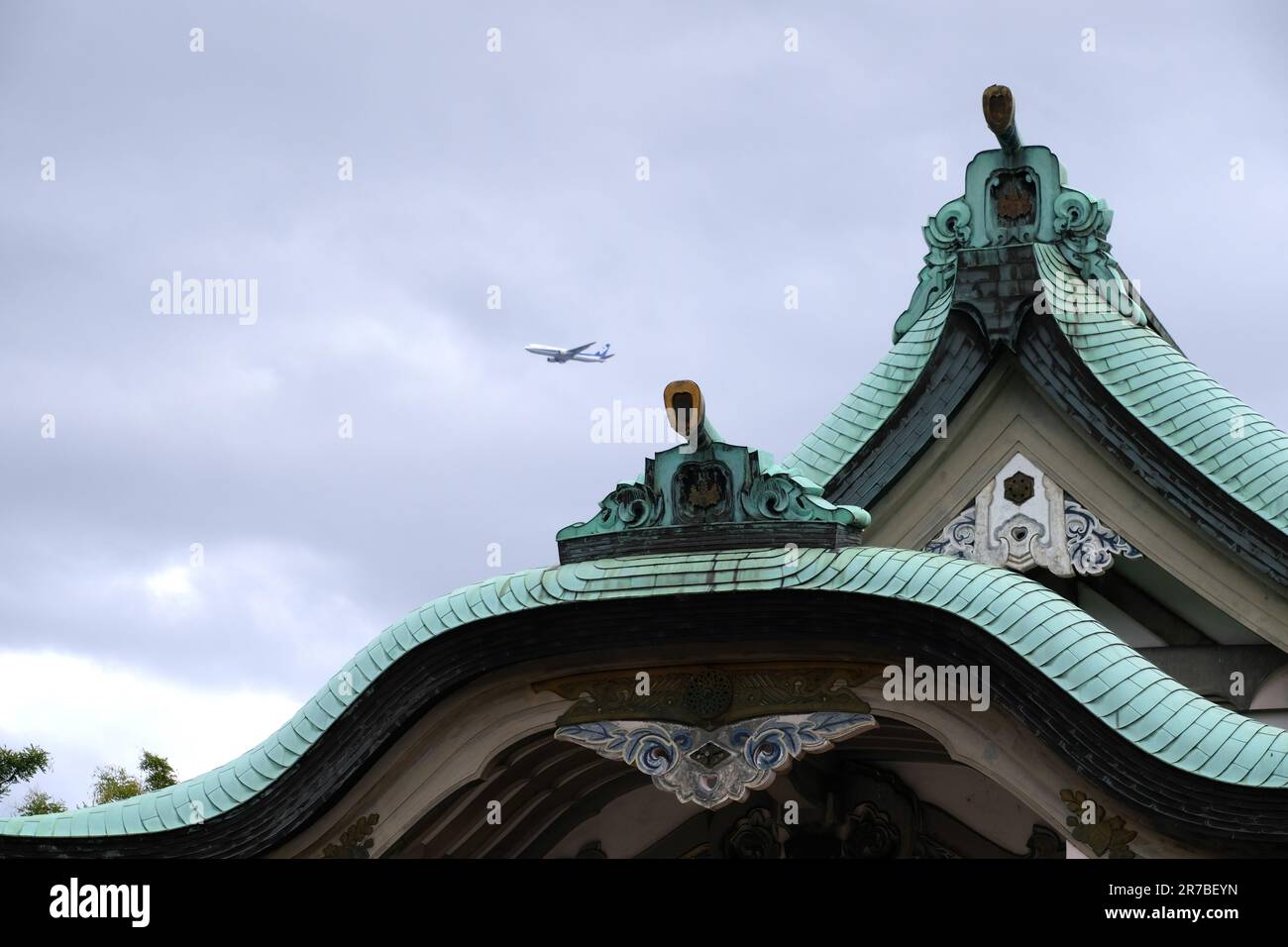 A traditional Asian roof with a commercial aircraft soaring in the sky ...