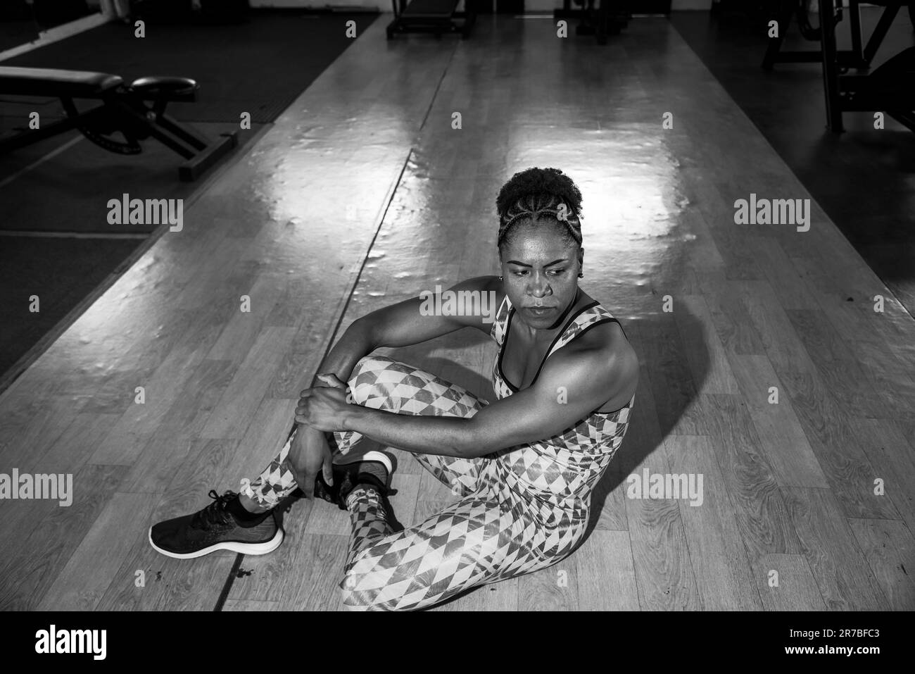 An African American female is exercising in a gym, sitting on the floor ...