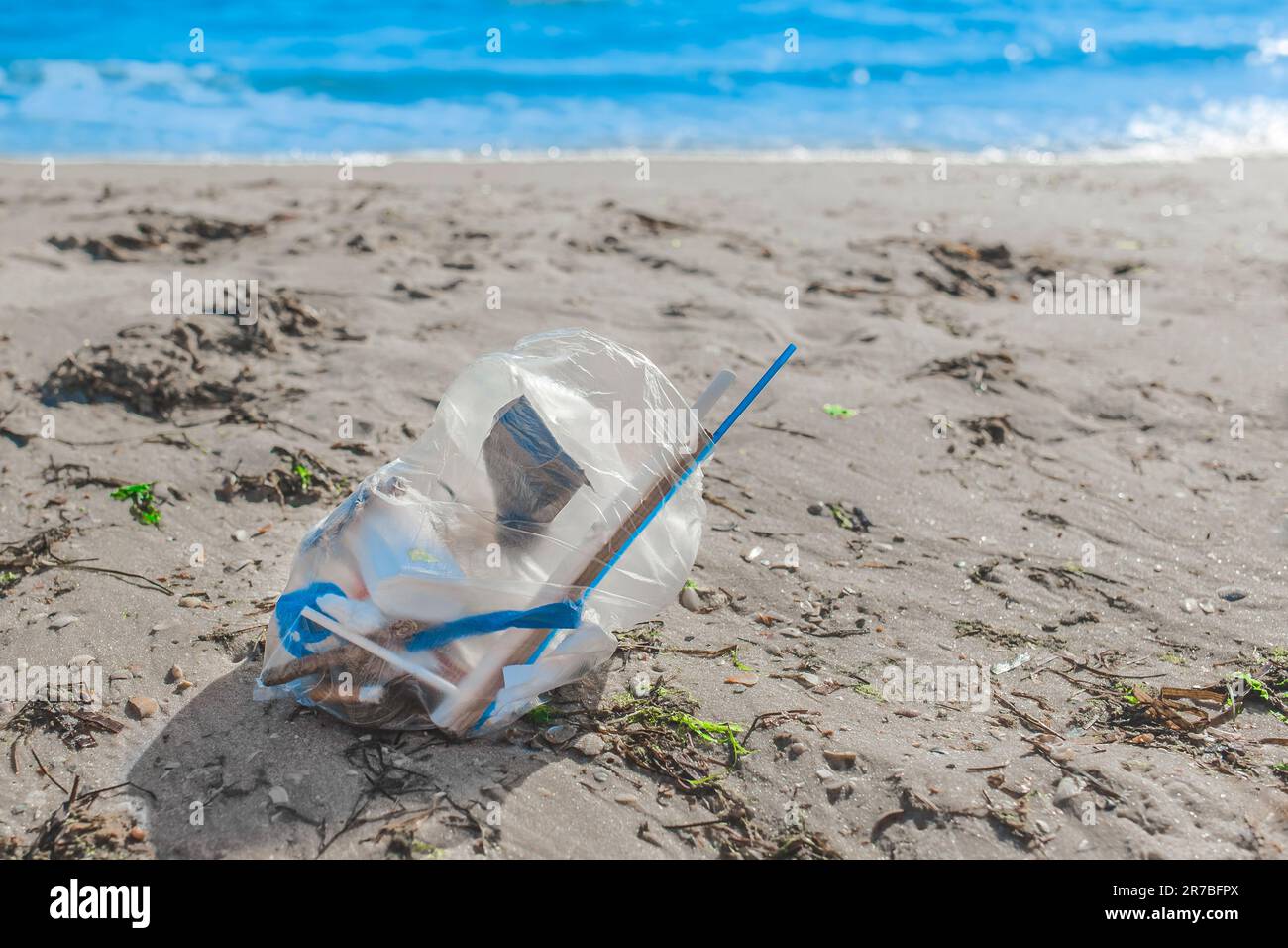 A pile of waste in a package lies on the beach sand against the sea ...