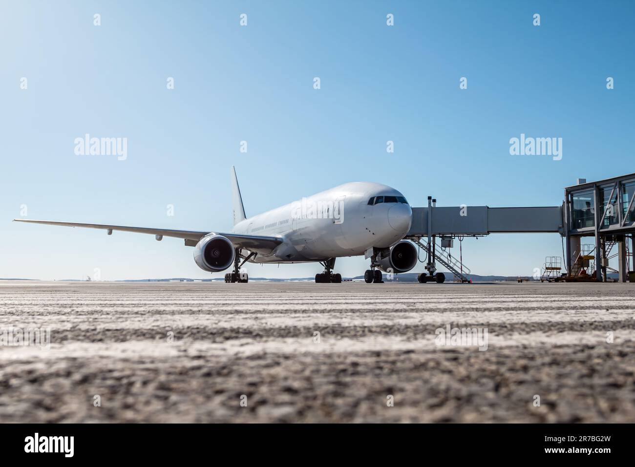 White wide body passenger airliner at the jetway on the airport apron ...