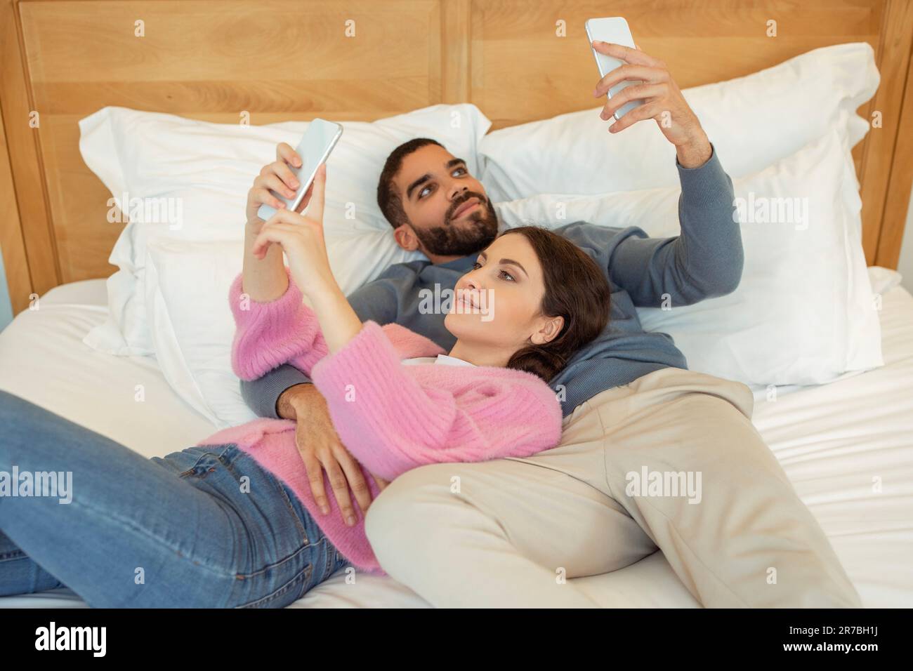 Young Married Couple Using Smartphones Lying In Bed At Home Stock Photo ...