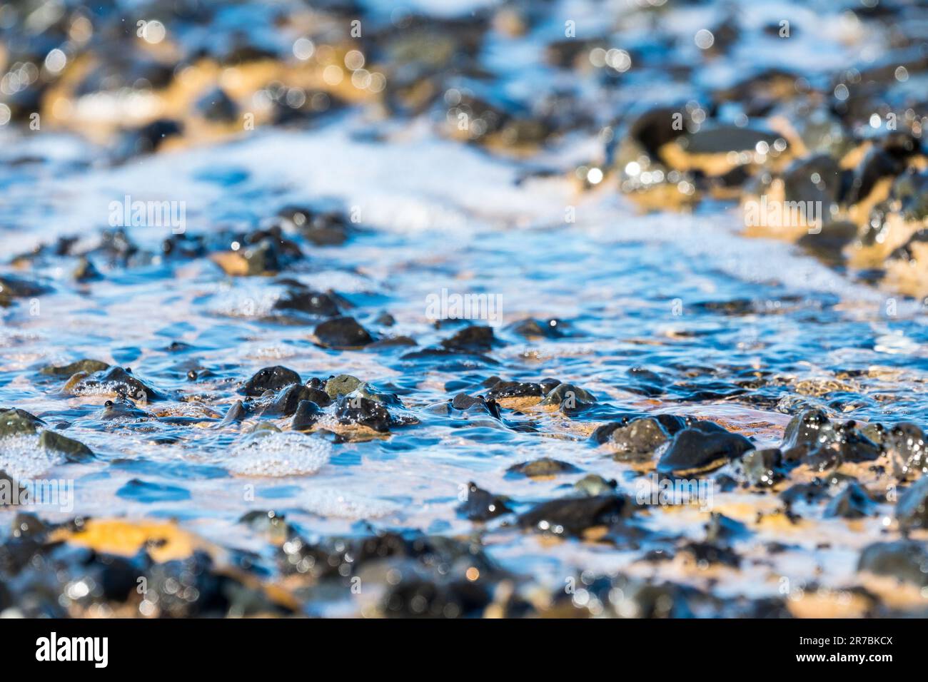small pebbles, rocks, stones surrounded by frothy sea water with ...