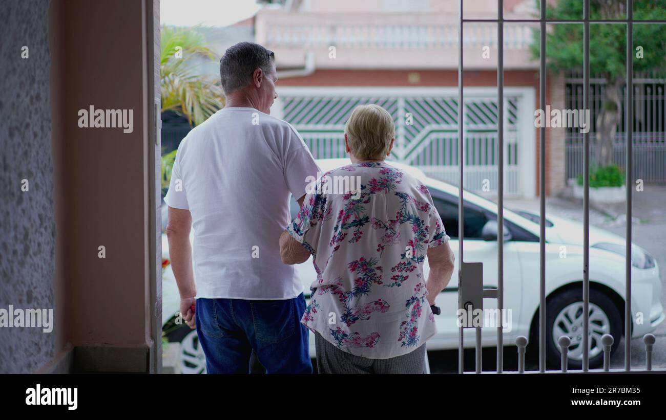 Adult son leaving home with his elderly mother to go for a walk ...