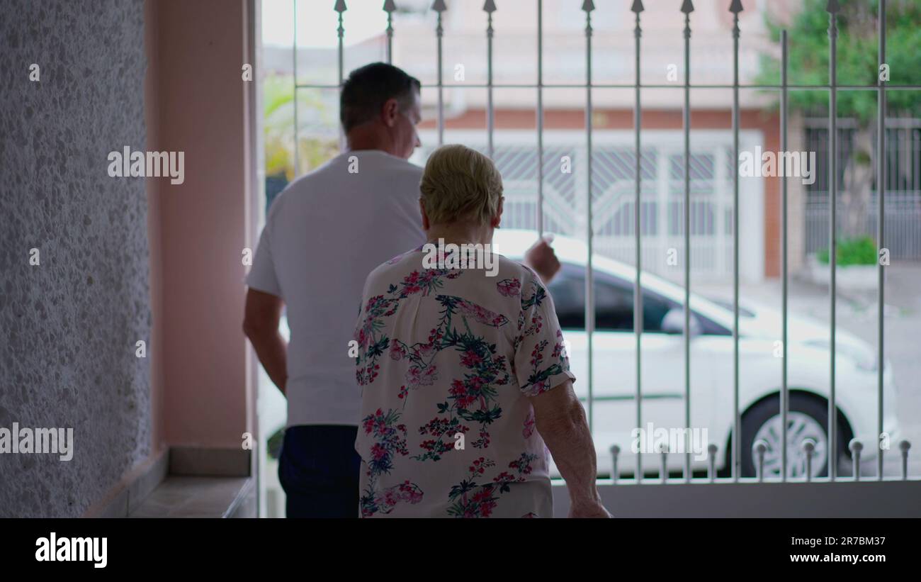 Adult son leaving home with his elderly mother to go for a walk ...