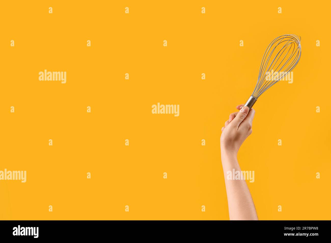 Female hand holding whisk on yellow background Stock Photo - Alamy