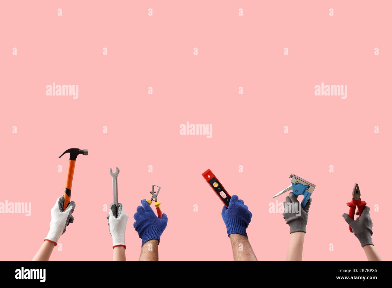 Female and male hands holding different construction tools on pink ...