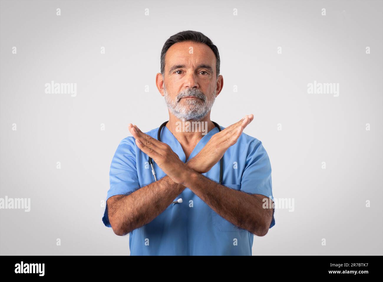 Serious caucasian senior doctor surgeon in blue uniform crossed arms ...