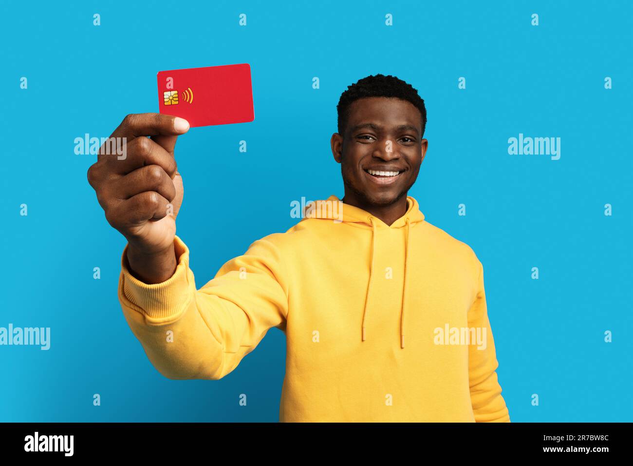 Happy young black guy showing bank card, blue background Stock Photo ...
