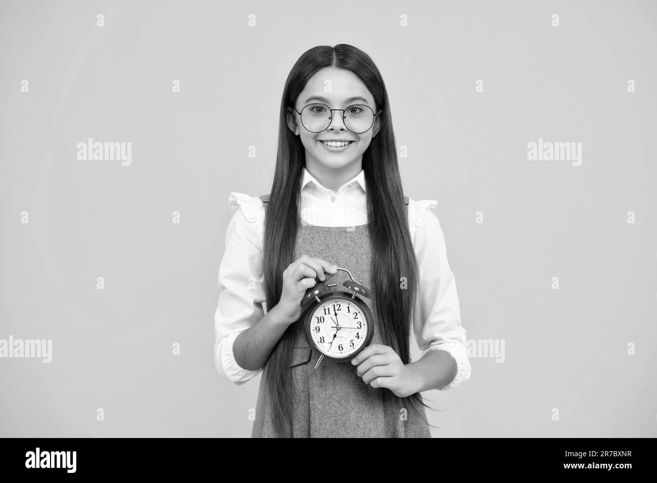 Teenager child hold clock isolated on yellow studio background ...