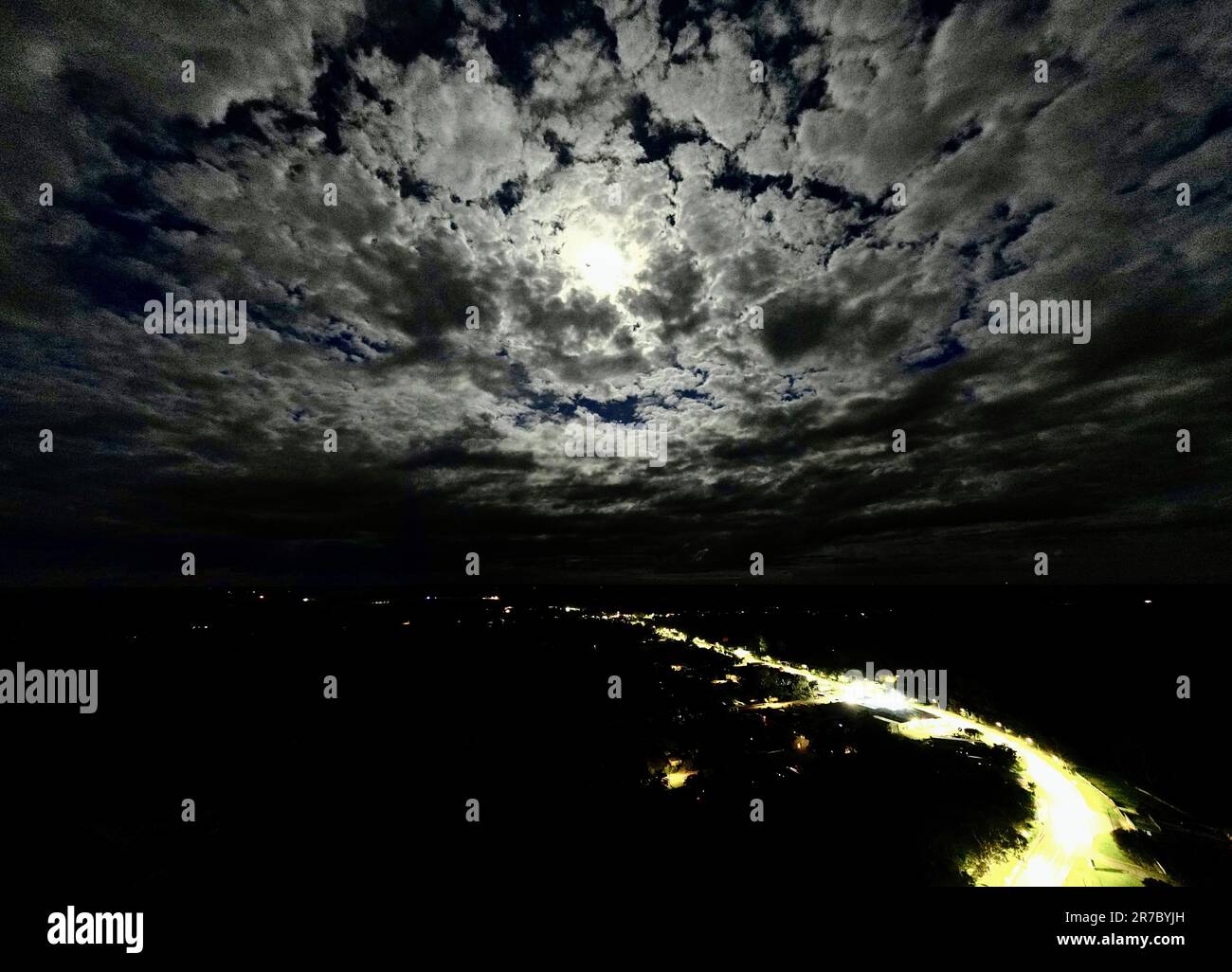 A tranquil landscape of a cloudy night sky with a setting moon above a ...