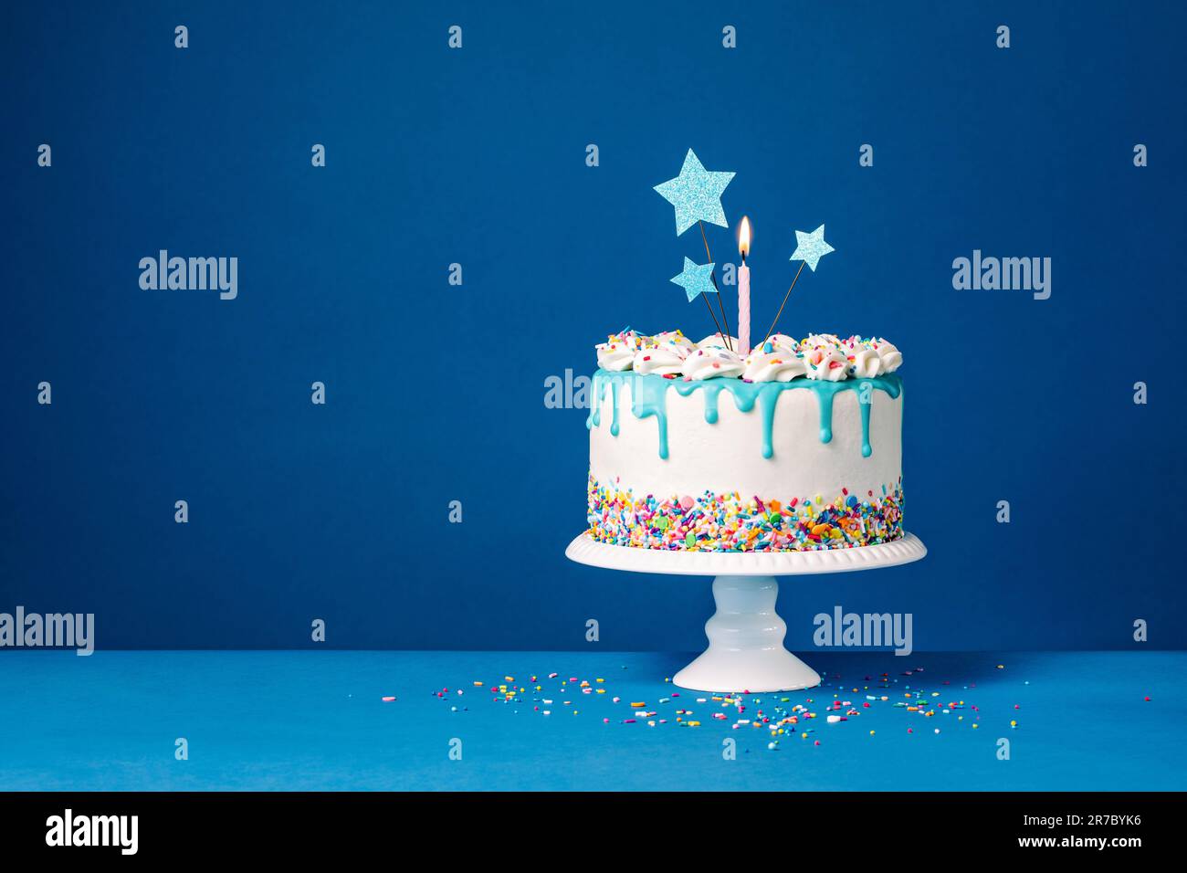 White Birthday drip cake with three star toppers, a candle and colorful ...