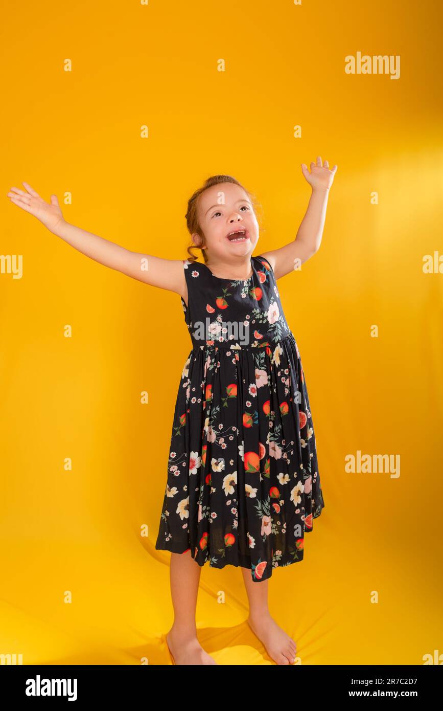 A Caucasian girl wearing a patterned dress stands with her hands raised ...