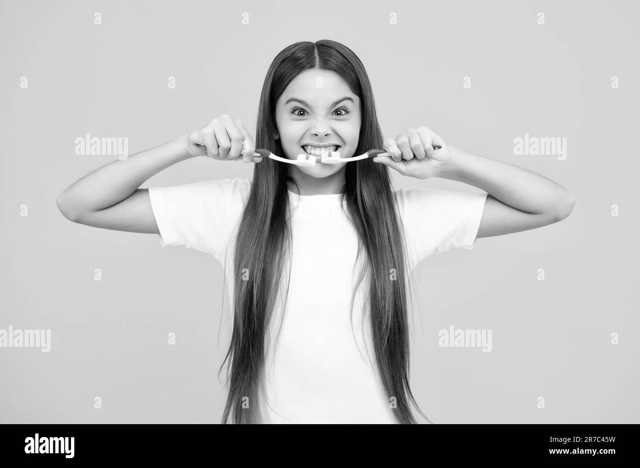 Funny face. Teenager girl brushing her teeth over isolated yellow ...