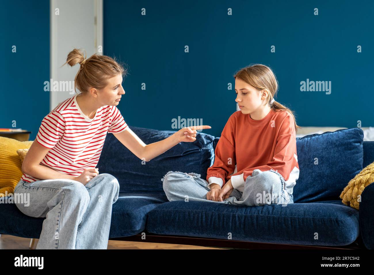 Angry mother pointing upset child sitting on sofa in living room. Conflict children and parents ...