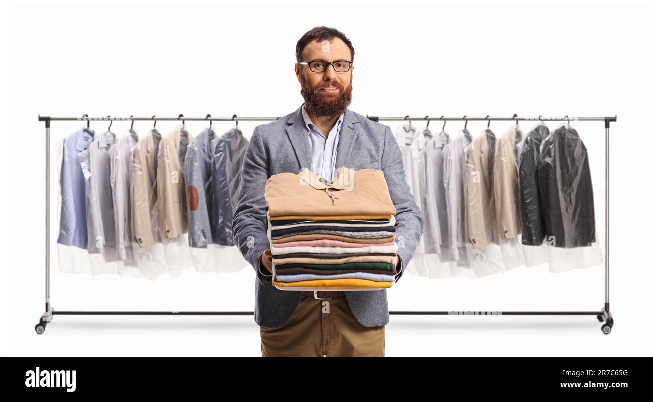 Bearded man holding a pile of folded clothes in front of clothing racks ...